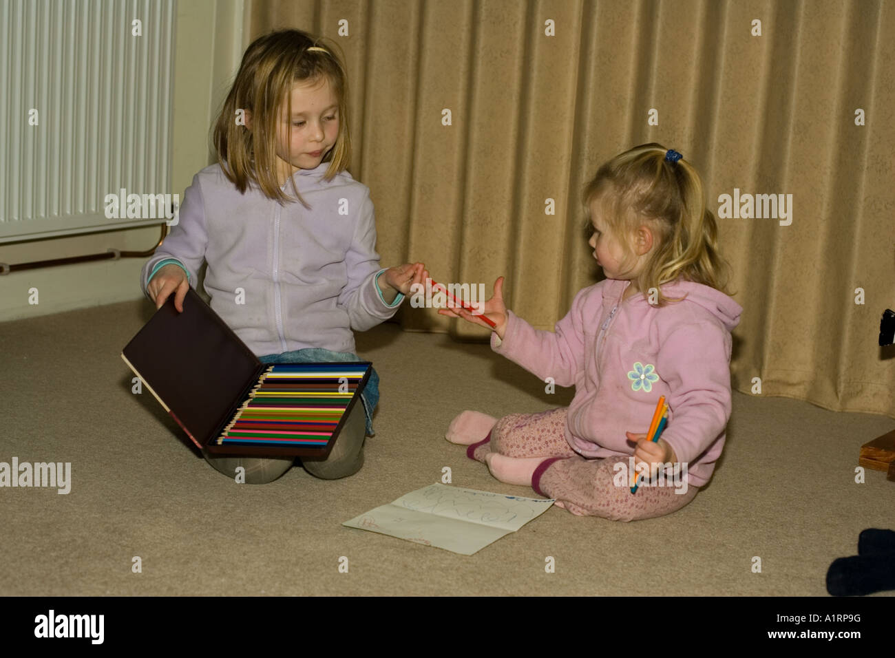 Six year old girl giving pencil to her two year old sister UK Stock ...