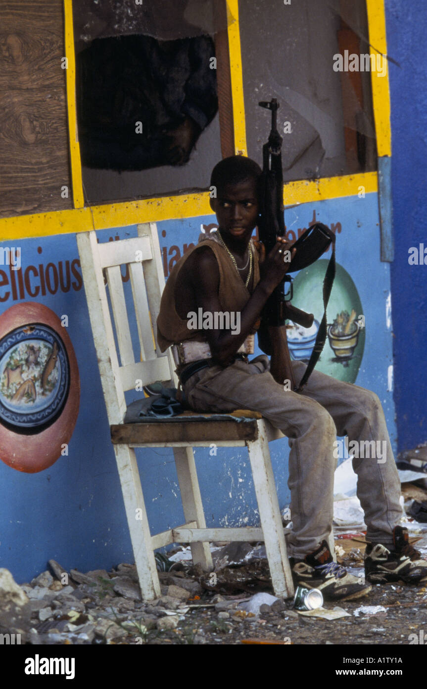 Young boy with a kalashnikov gun guarding a restaurant with a broken ...