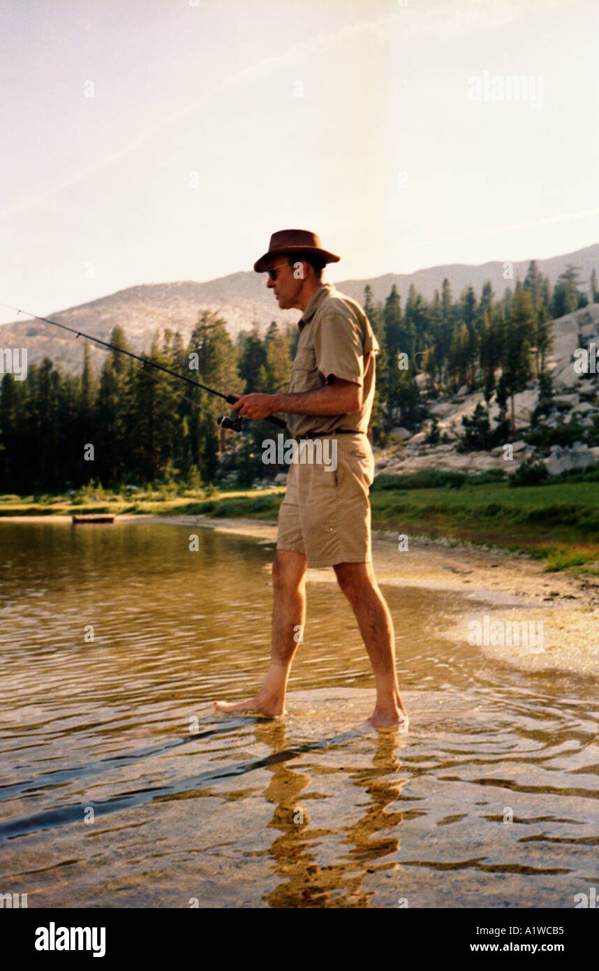 a man walking into a lake to go fishing after a day of backpacking ...