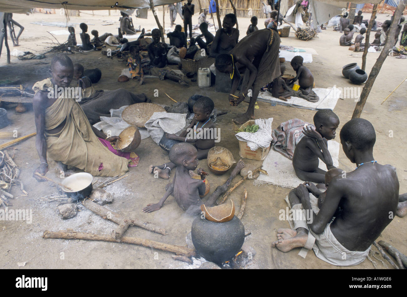 EMACIATED WOMAN COOKING ON OPEN FIRE SURROUNDED BY OTHERS SUFFERING ...