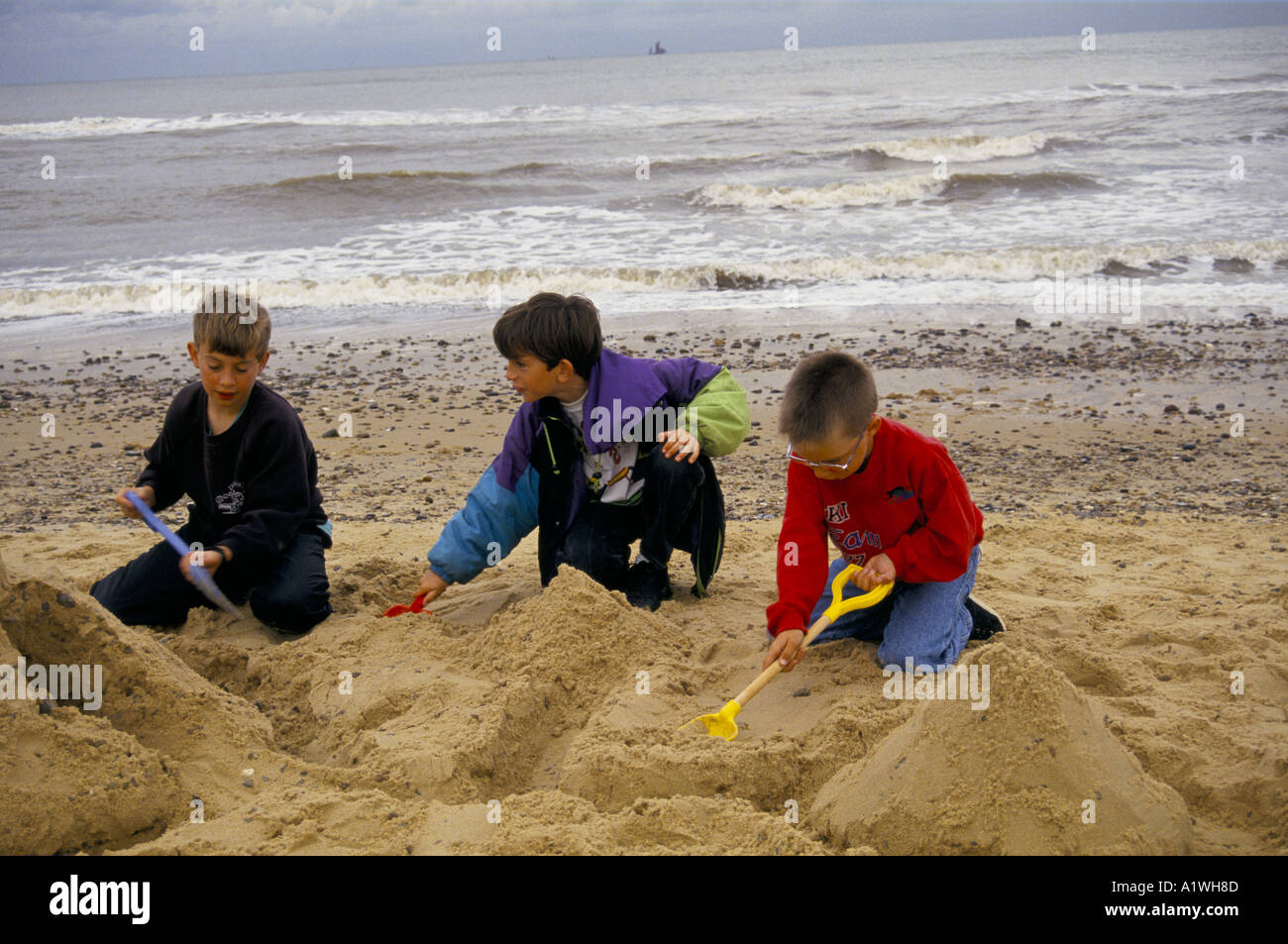 BOYS DIGGING MOAT AND BUILDING SANDCASTLES WHILST PLAYING ON THE BEACH ...