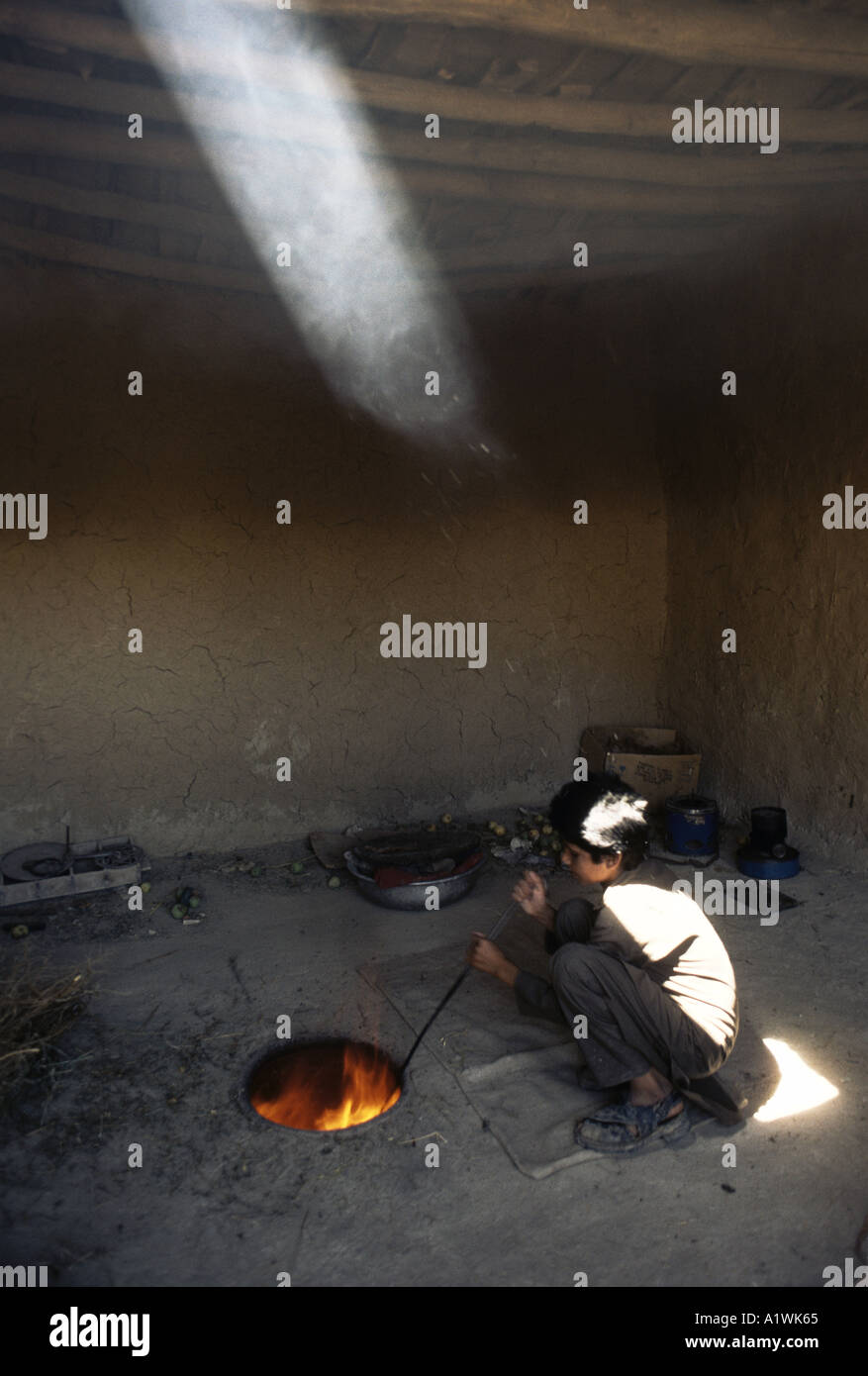 VILLAGE KITCHEN.Boy cooking on a traditional tandoor, a fire pit ...