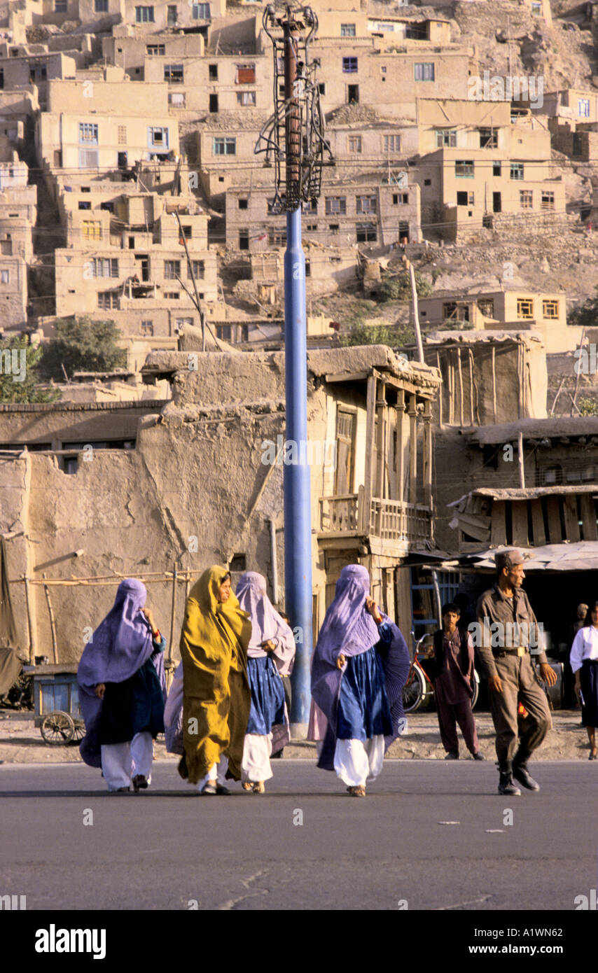 Group of women in burqas cross the street in front of a hillside ...