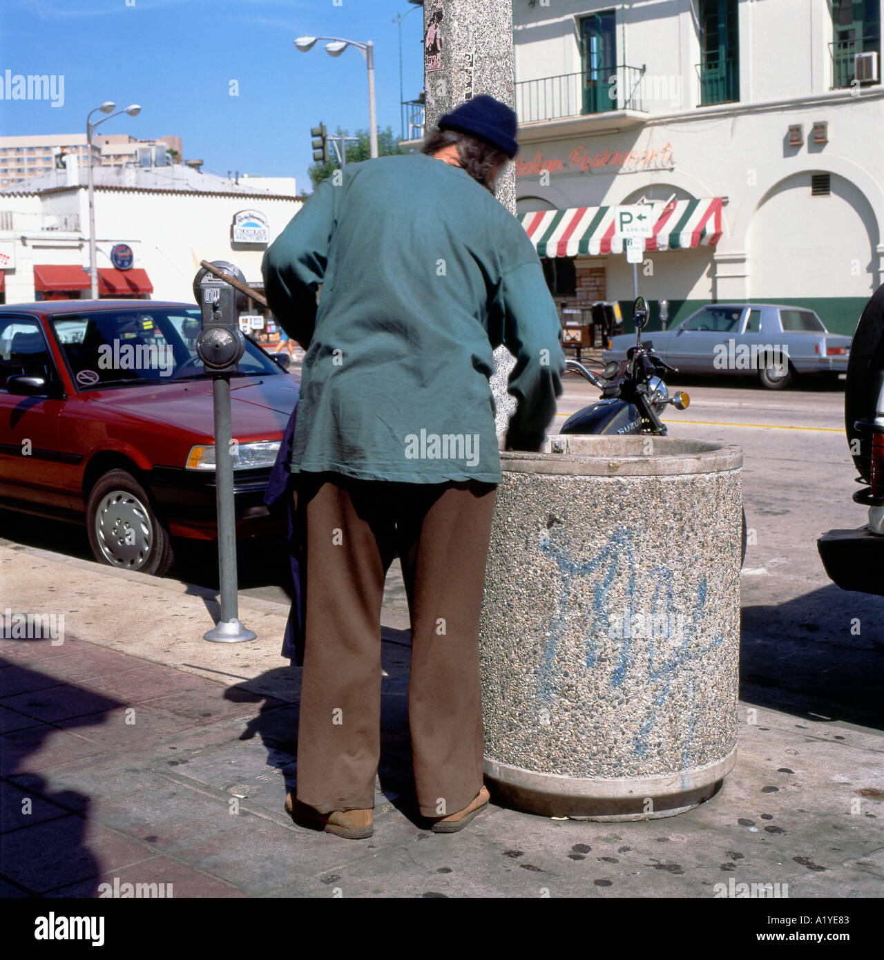 A homeless man looking through a garbage can bin in affluent area of ...