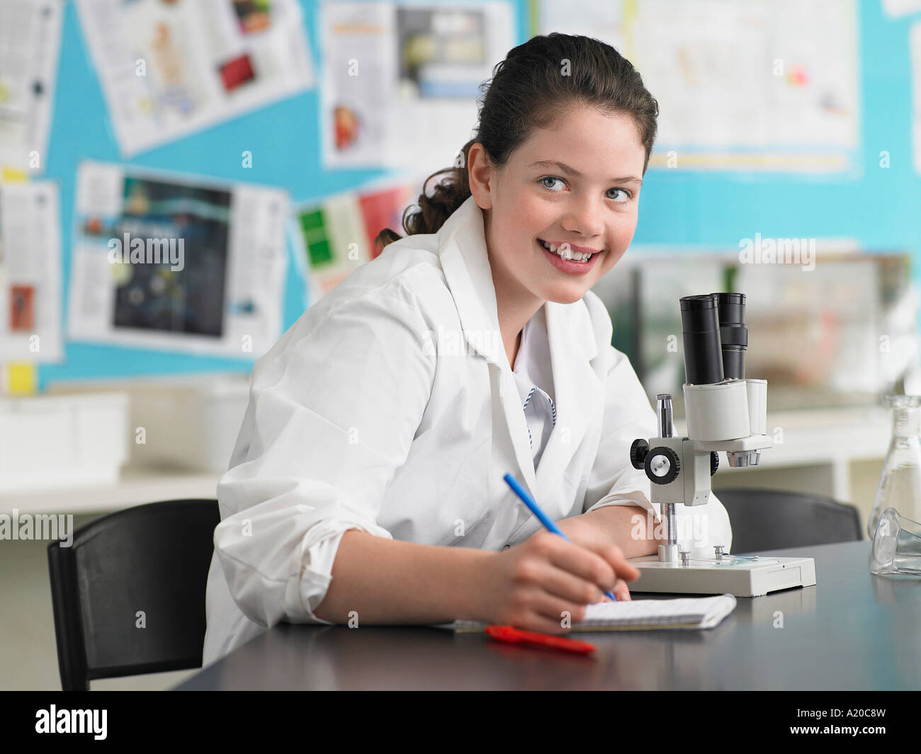 Teenage girl using microscope and taking notes in classroom, portrait ...