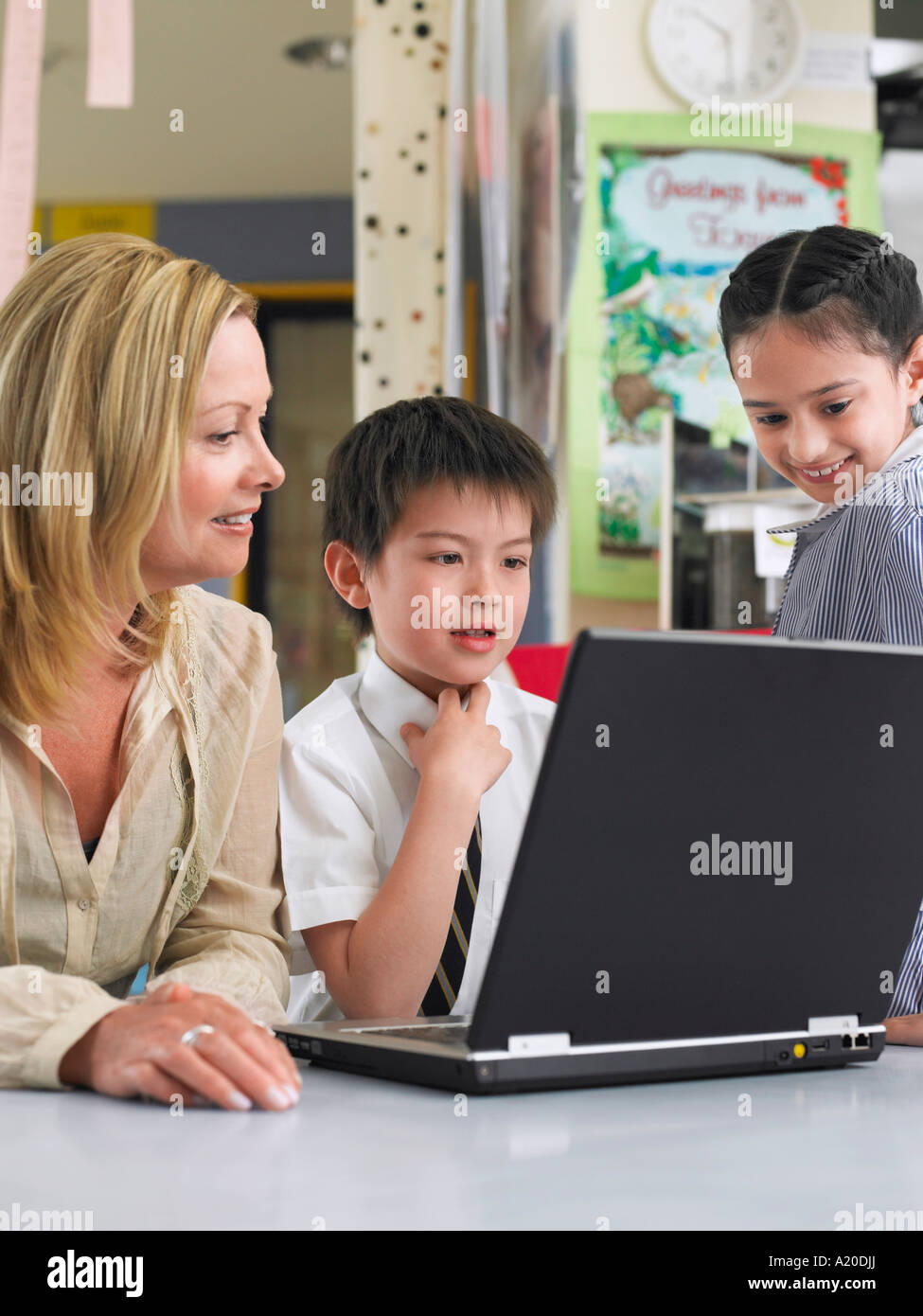 Teacher sitting with students using laptop in classroom Stock Photo - Alamy