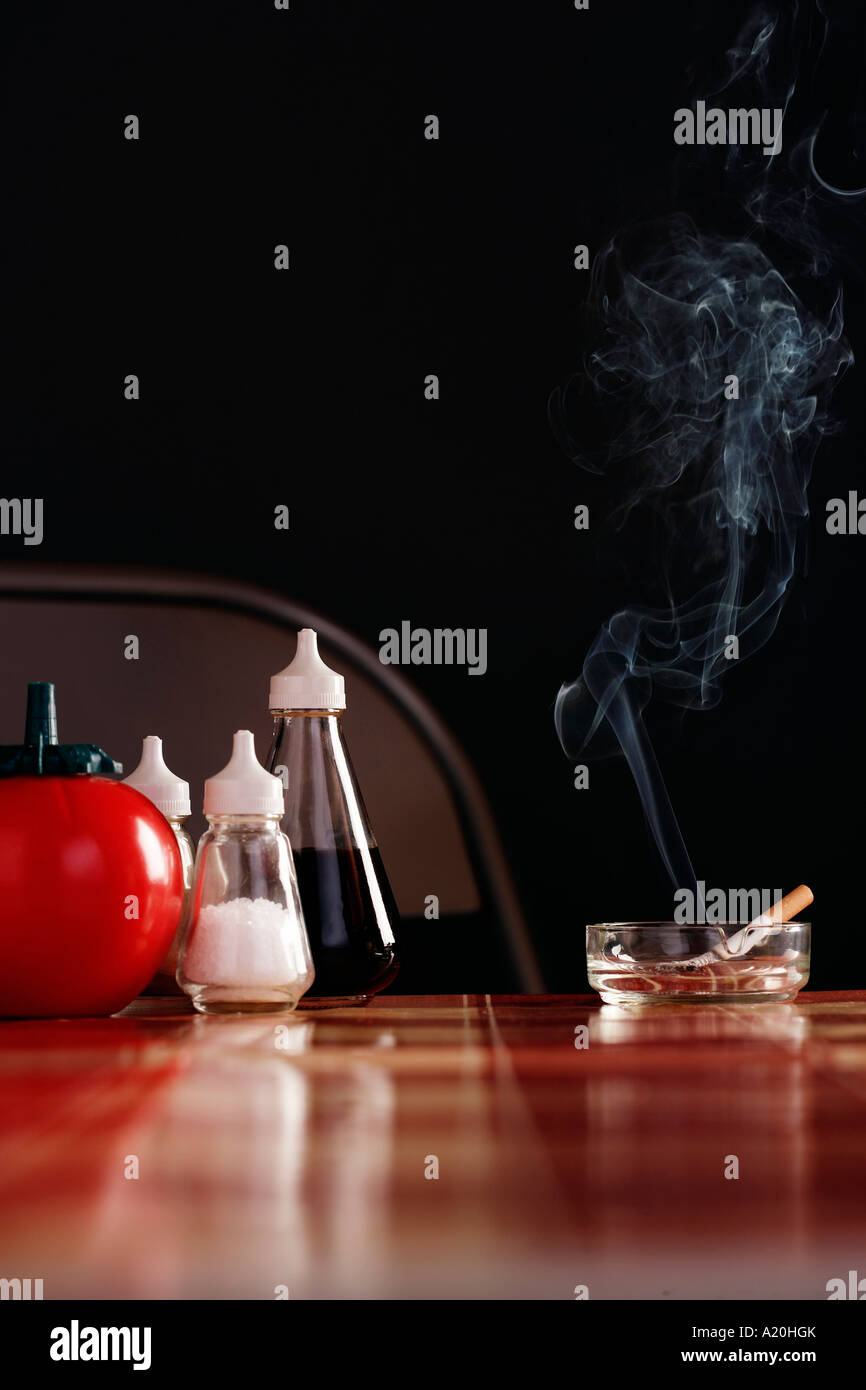 Smoking cigarette in ashtray on table with condiments Stock Photo - Alamy