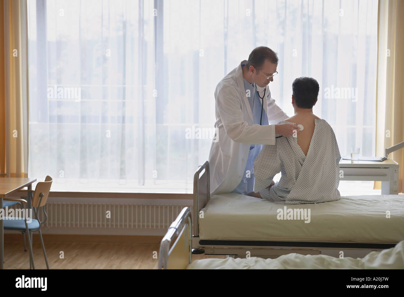 Doctor using stethoscope on back of patient in hospital room, back view ...