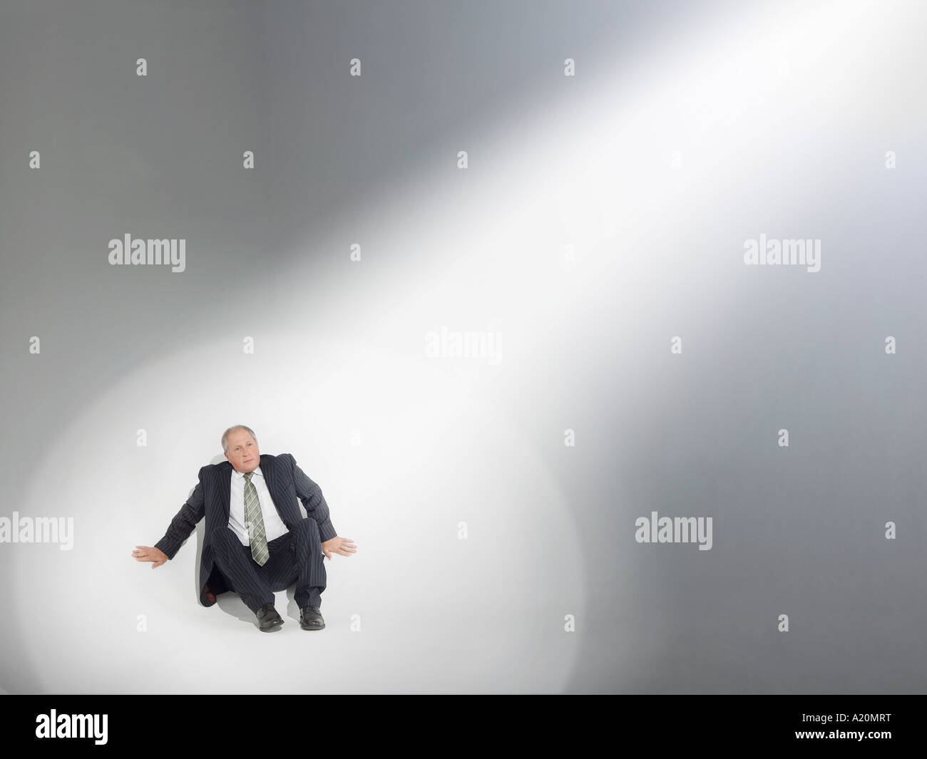Businessman sitting, looking up at source of spotlight Stock Photo - Alamy