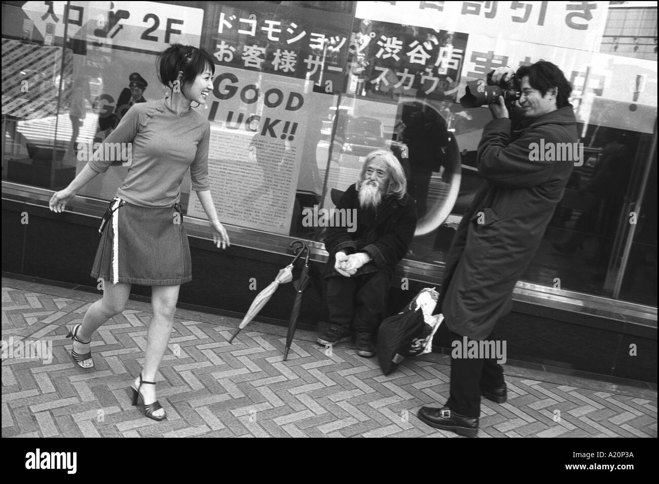 A model gets photographed by a photographer whilst a homeless man sits ...