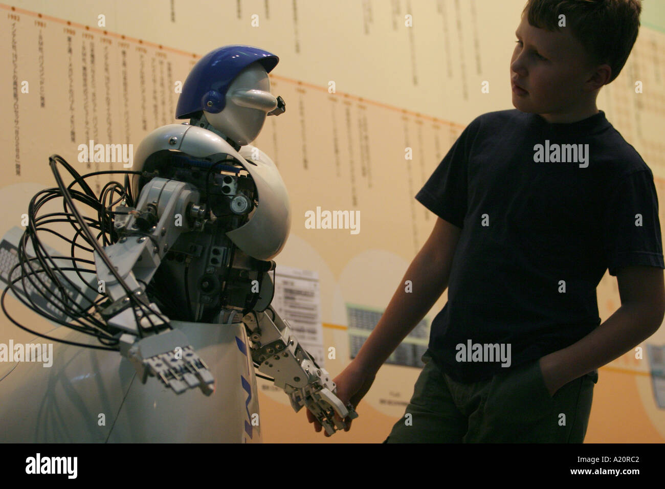 A young boy holds hands with the Tmsuk 4 Humanoid robot made by Tmsuk ...