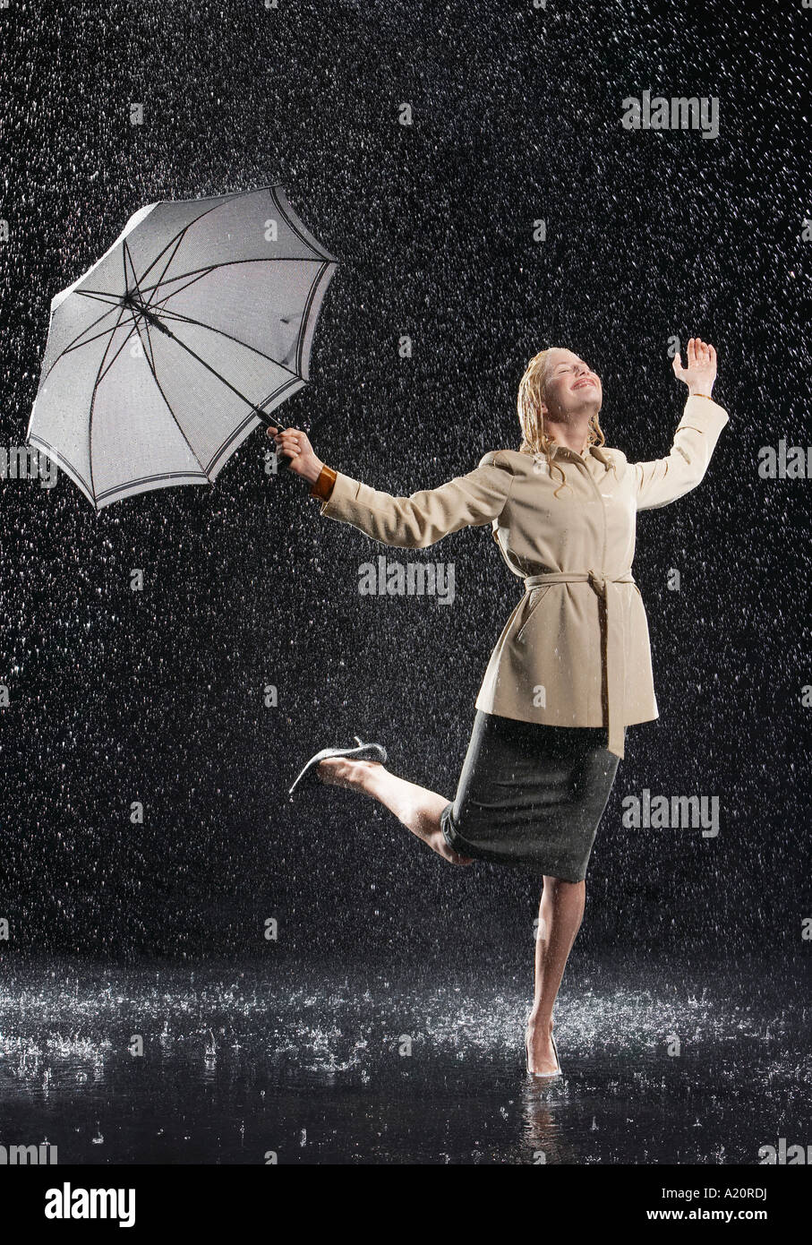 Woman standing on one leg, holding umbrella, leaning into falling rain ...