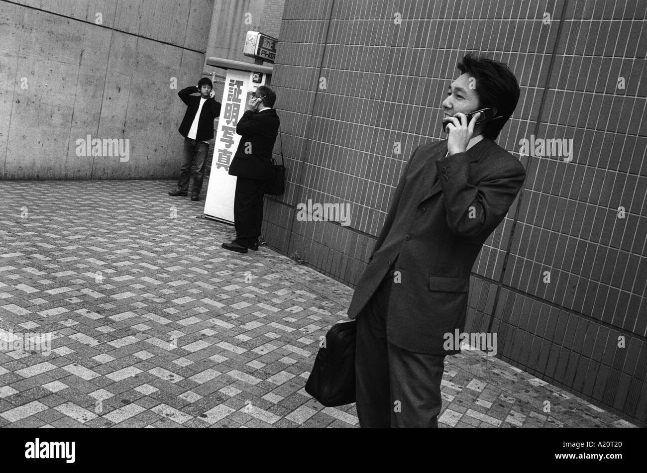 Japanese men use their mobile telephones on the street of Tokyo, Japan ...