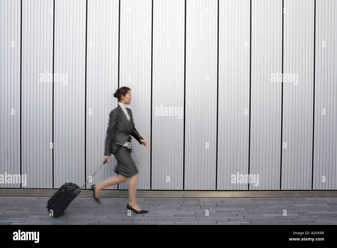 Businesswoman walking outdoors, pulling suitcase behind her, side view ...