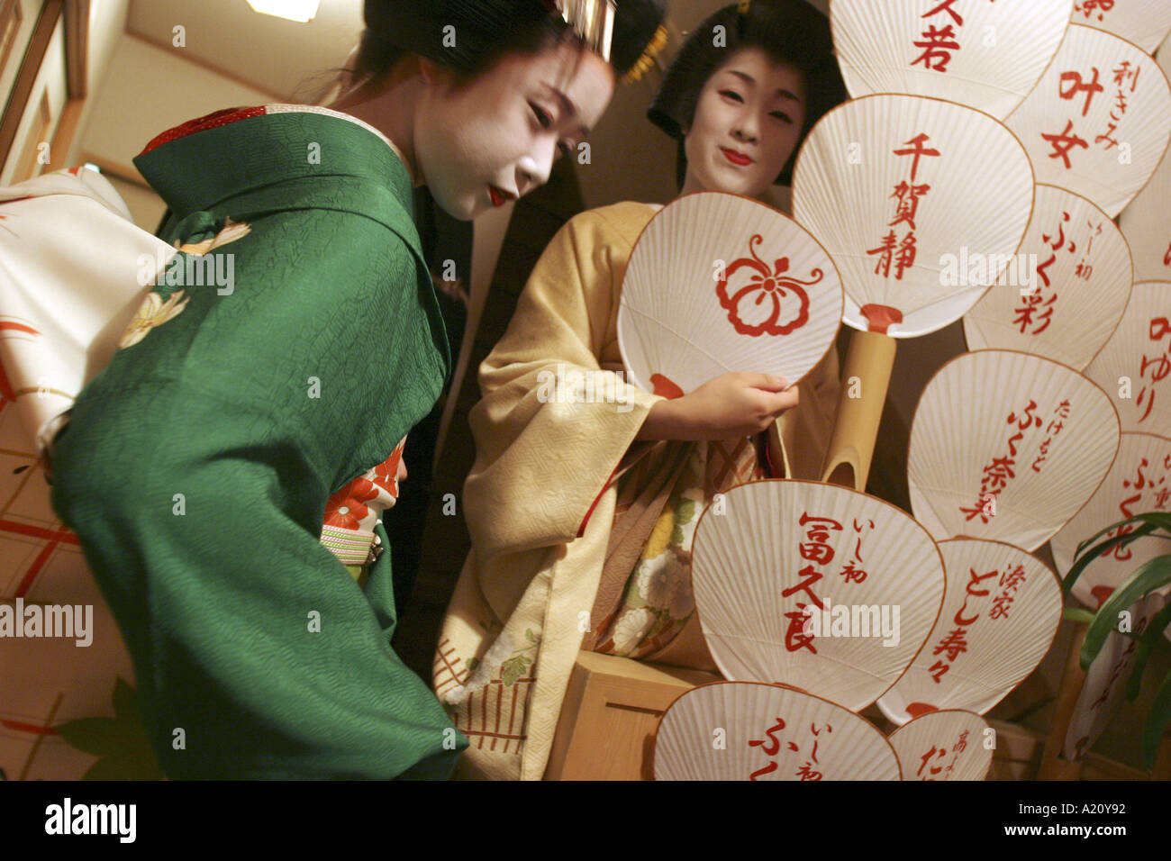 Geisha and maiko girls at entrance to tea house with fans, Kyoto, Japan ...