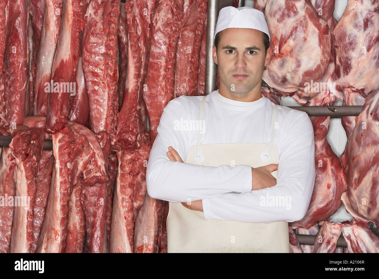 Butcher Standing, arms crossed, in front of raw meat in Meat Locker ...