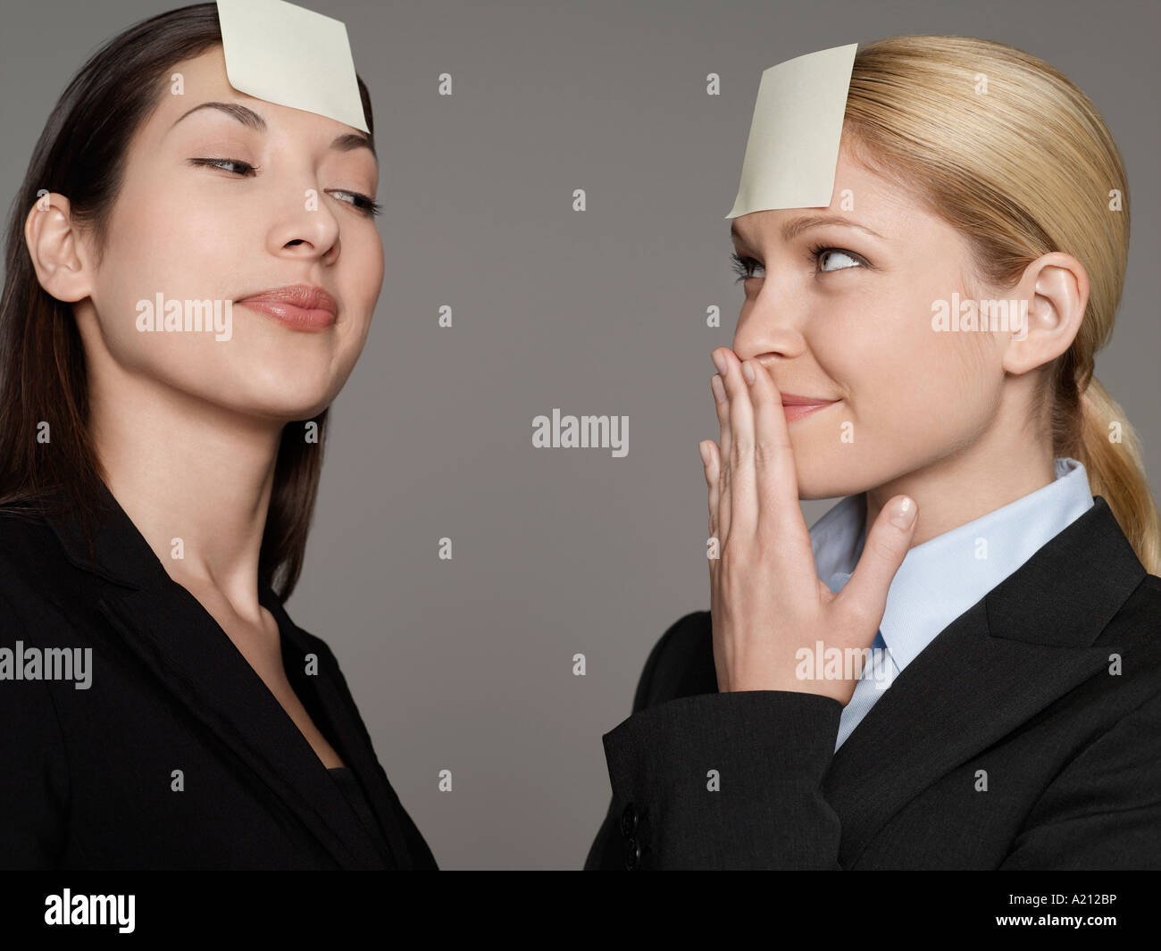 Two female office workers with sticky notes on foreheads against gray ...