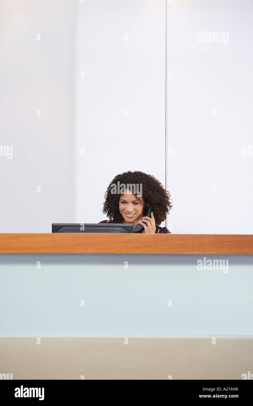 Receptionist sitting behind reception desk, talking on Telephone Stock ...