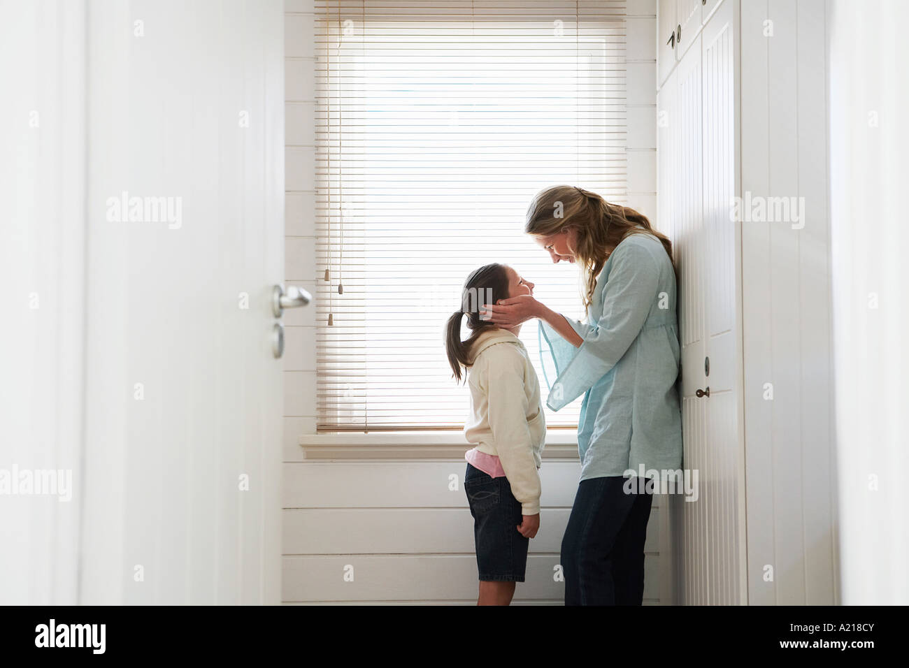 Mother cupping daughters face in hands, standing by window Stock Photo ...
