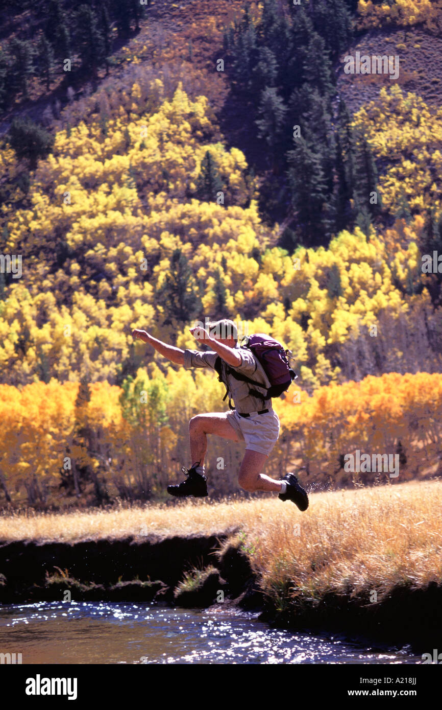 A man jumping over a creek in the autumn in the Sierra mountains of ...