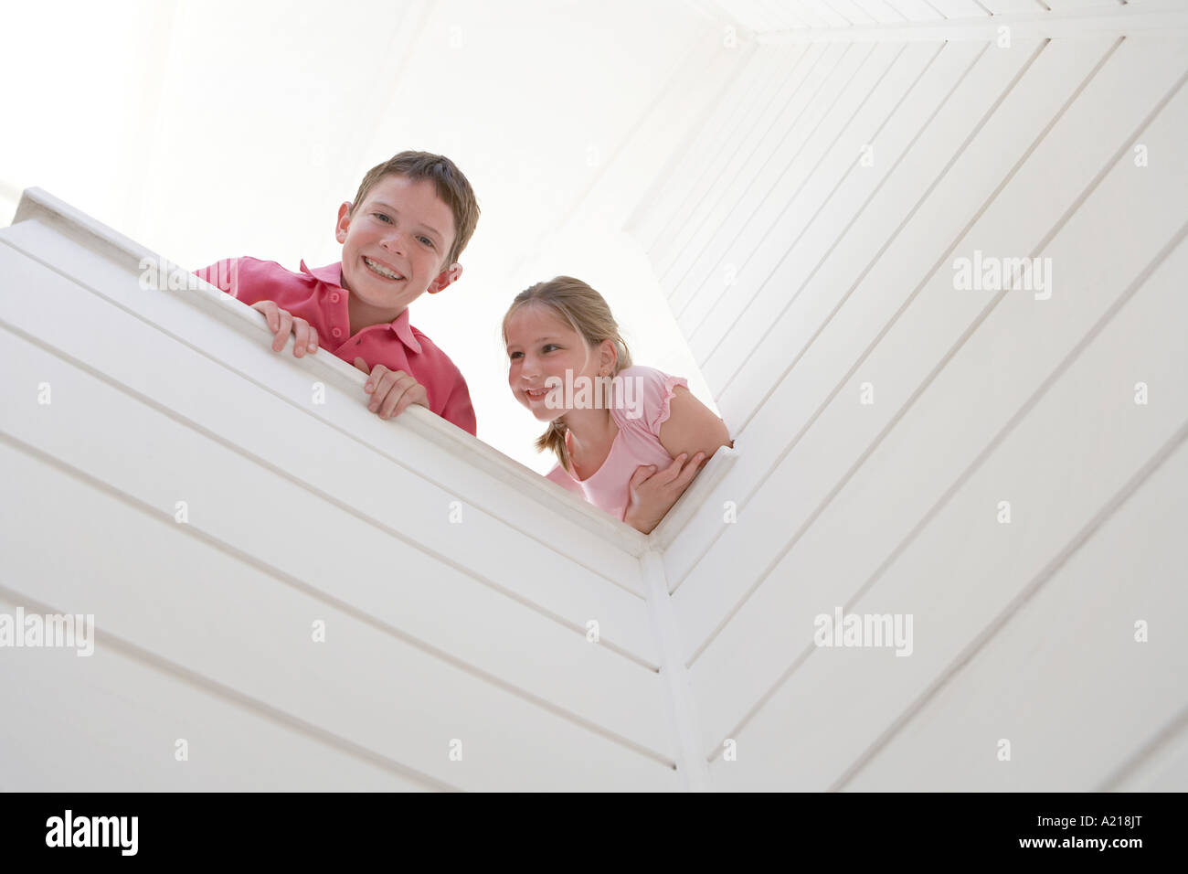 Young girl and boy looking over white wall, view from below Stock Photo ...