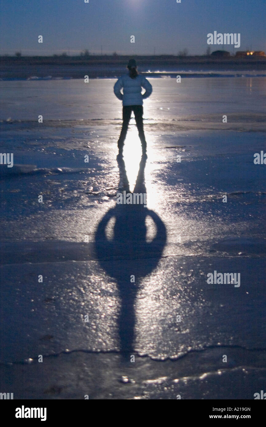 A woman standing on a frozen lake at night with her moon shadow in ...