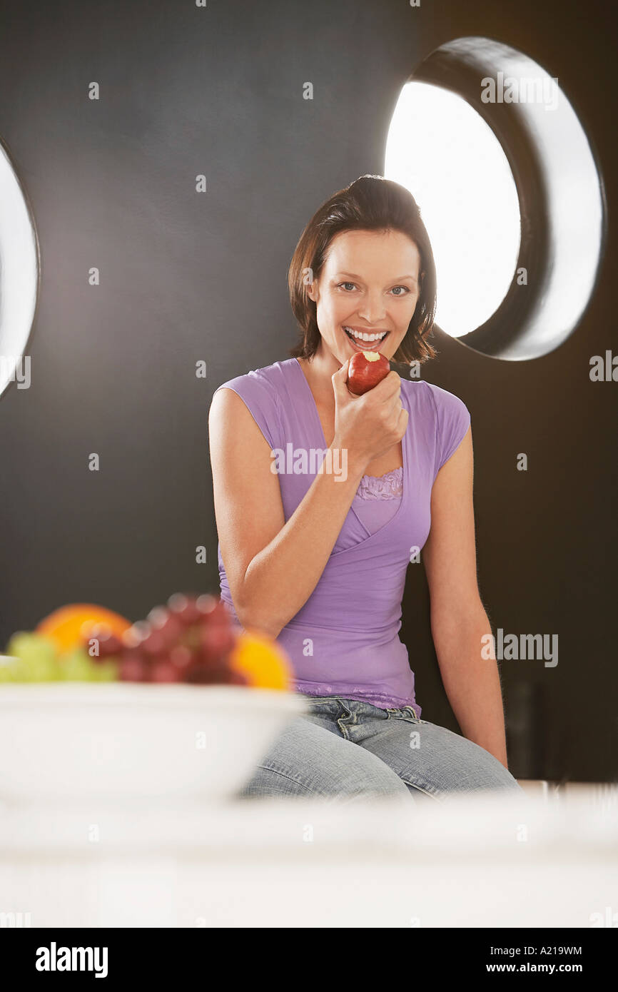 Woman eating apple, sitting on kitchen surface Stock Photo - Alamy