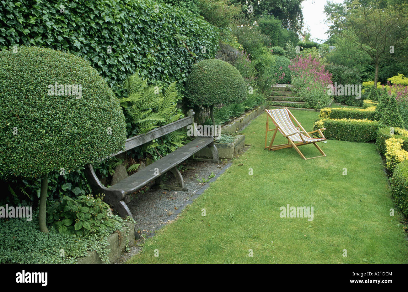 Deckchair on lawn in front of wooden bench between clipped shrubs in ...