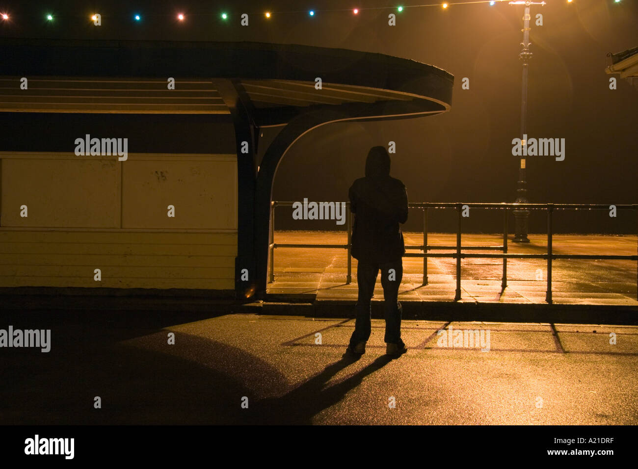 A lone silhouetted figure stands by a shelter in coastal town at night ...