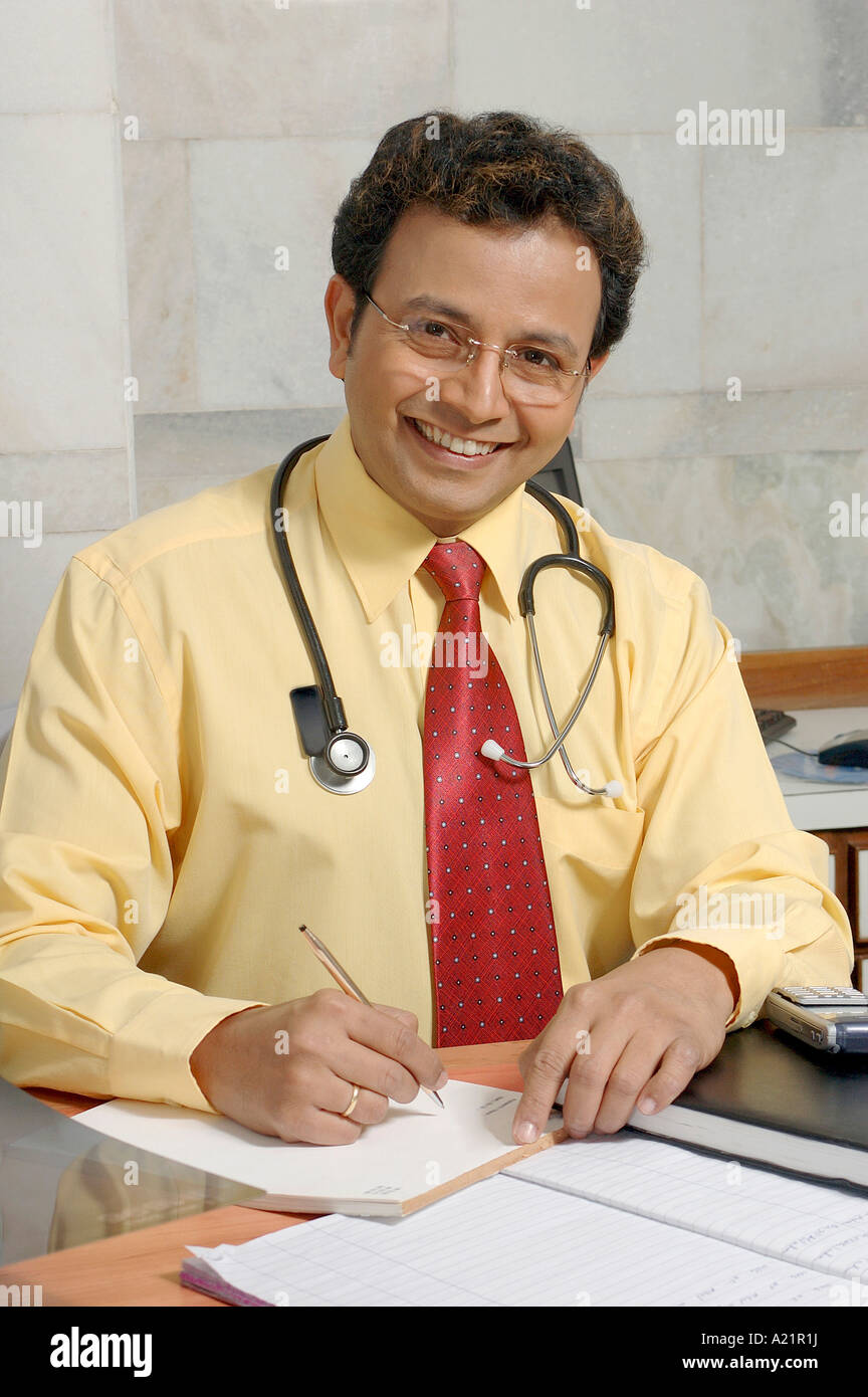 Young Indian Doctor smiling with stethoscope in clinic writing ...