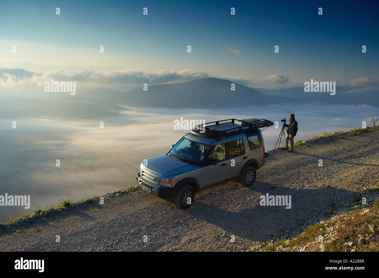 a photographer working beside a 4x4 vehicle Land Rover above the mist ...