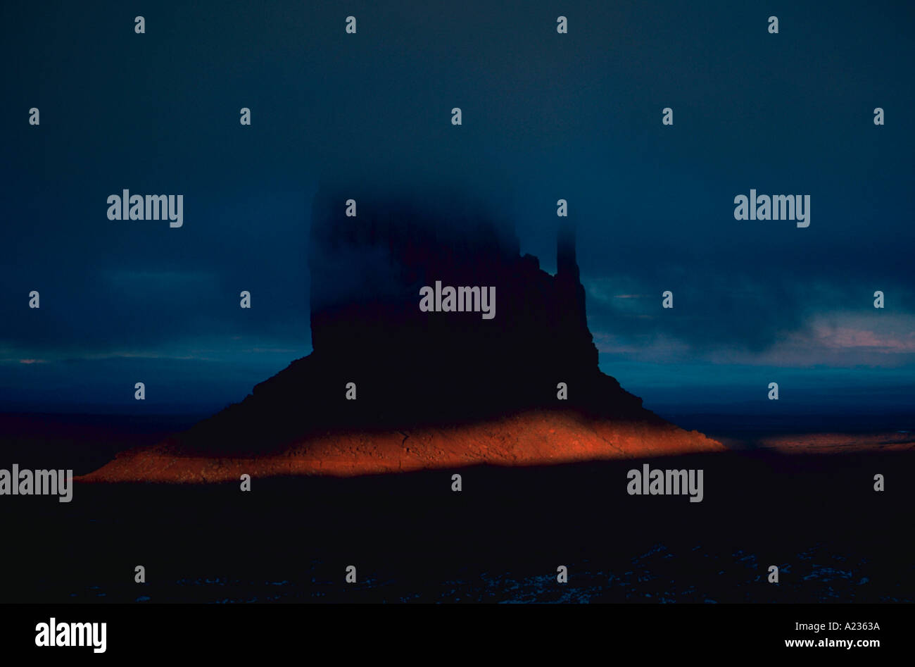 Mitten Buttes is lit by a crack of light at sunset beneath a deck of ...