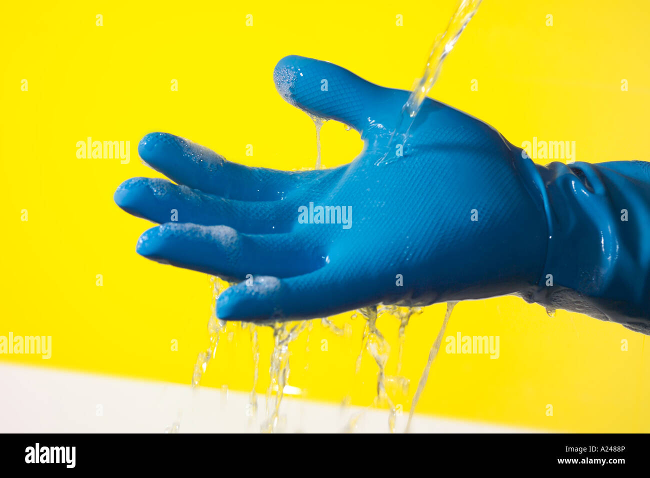 Hand in blue rubber glove with soap suds washing up protective glove ...