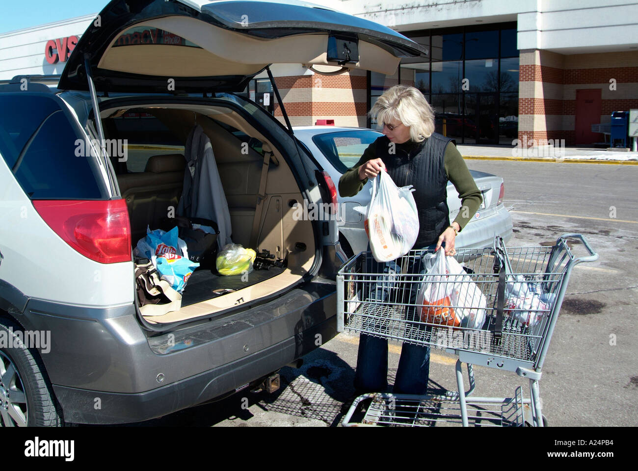 Adult female loads groceries into her car after shopping at a grocery ...