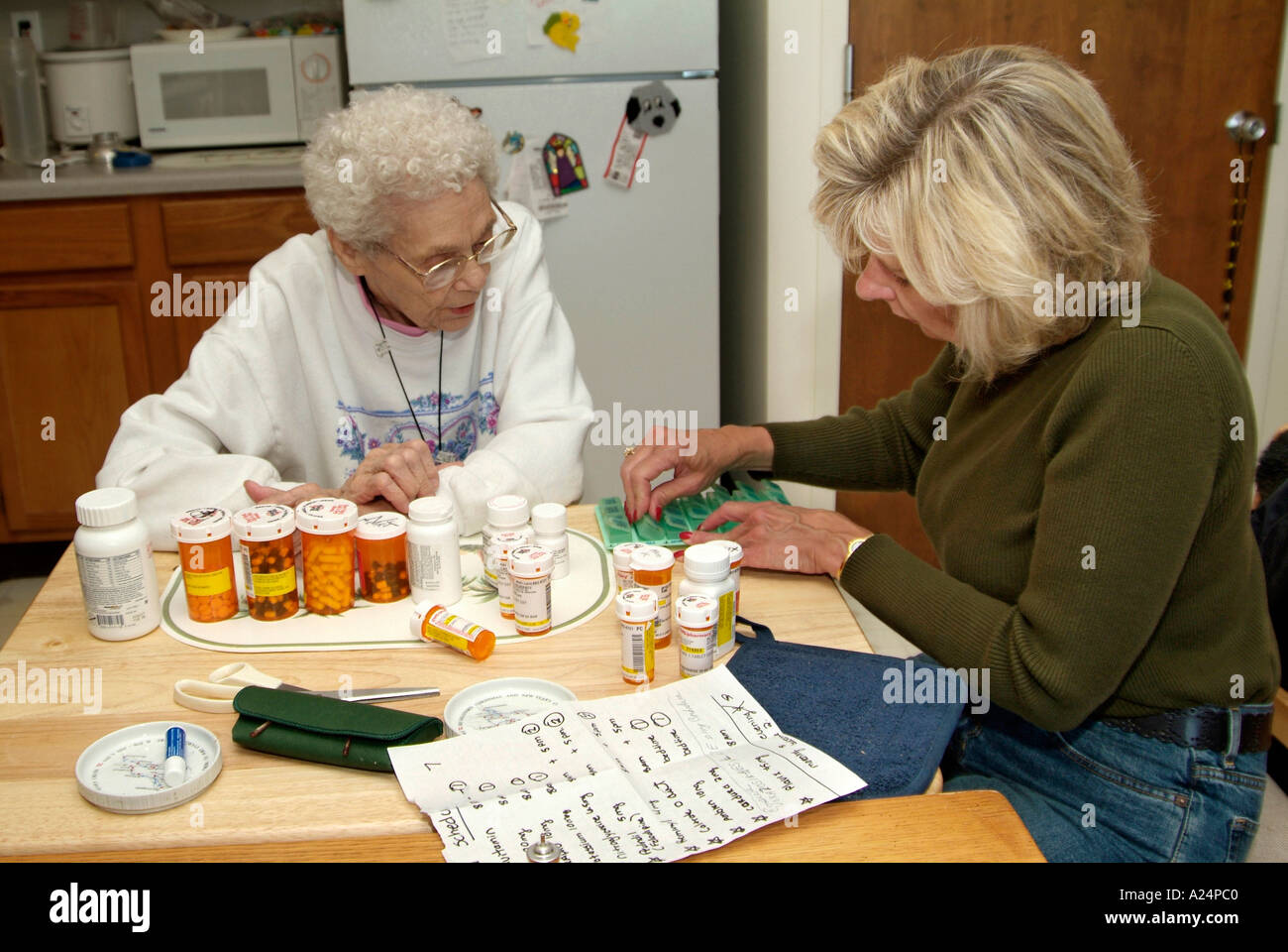 Middle age daughter helps 85 year old mother sort medication into a one ...