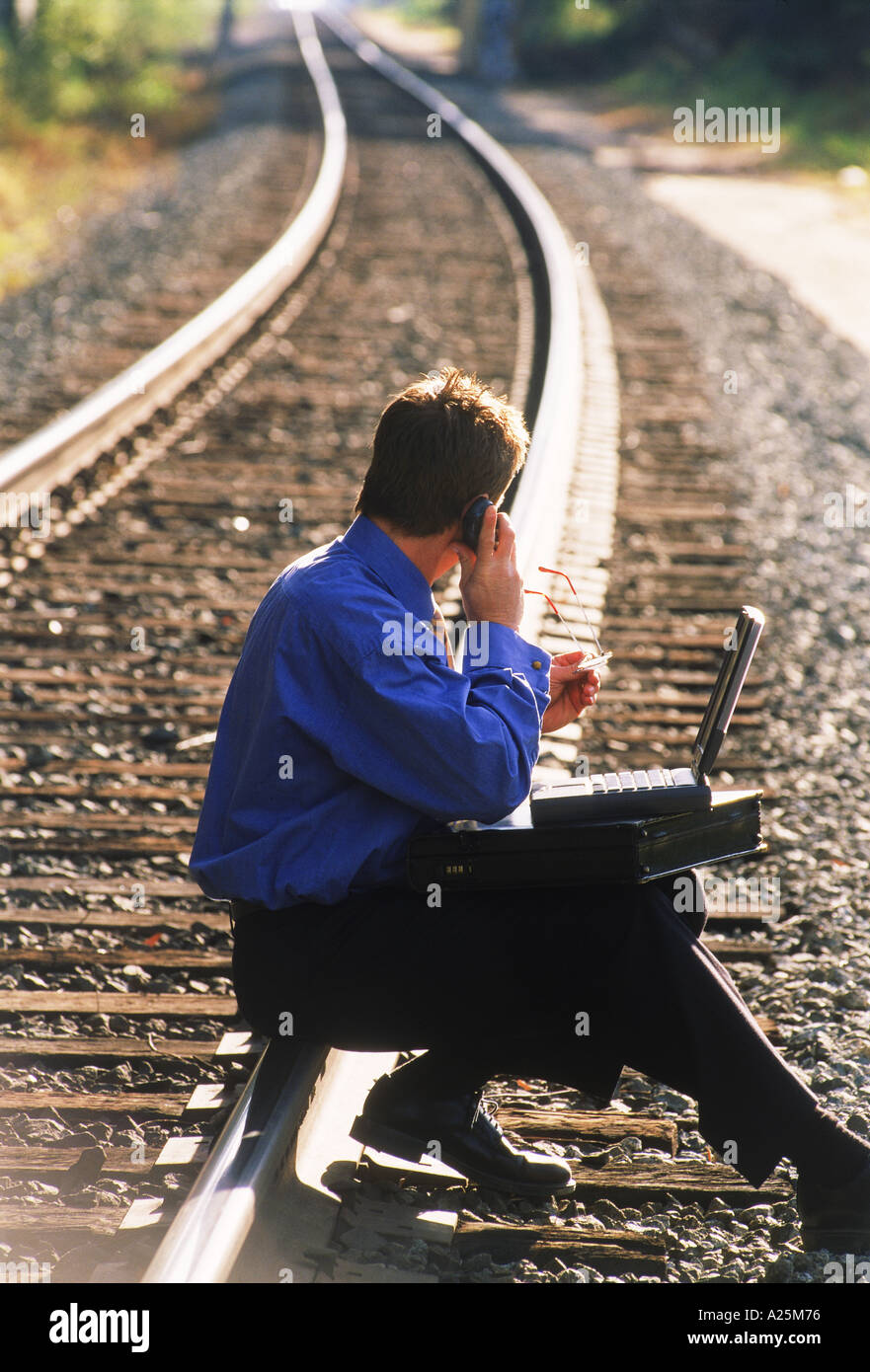 Businessman with laptop and cellphone sitting on railroad track Stock ...