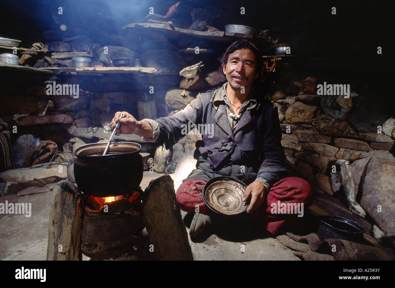 A DOLPO MAN COOKING FOOD with KITCHEN UTENSILS in a yak herder hut ...
