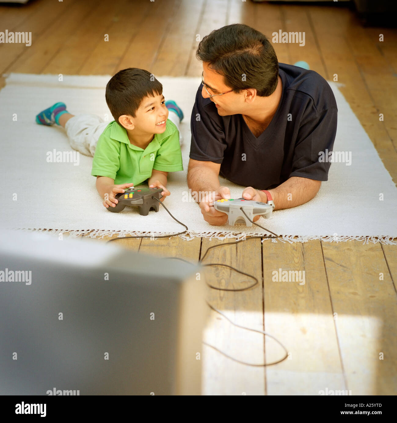 father and son playing video games together lying on a rug Stock Photo ...