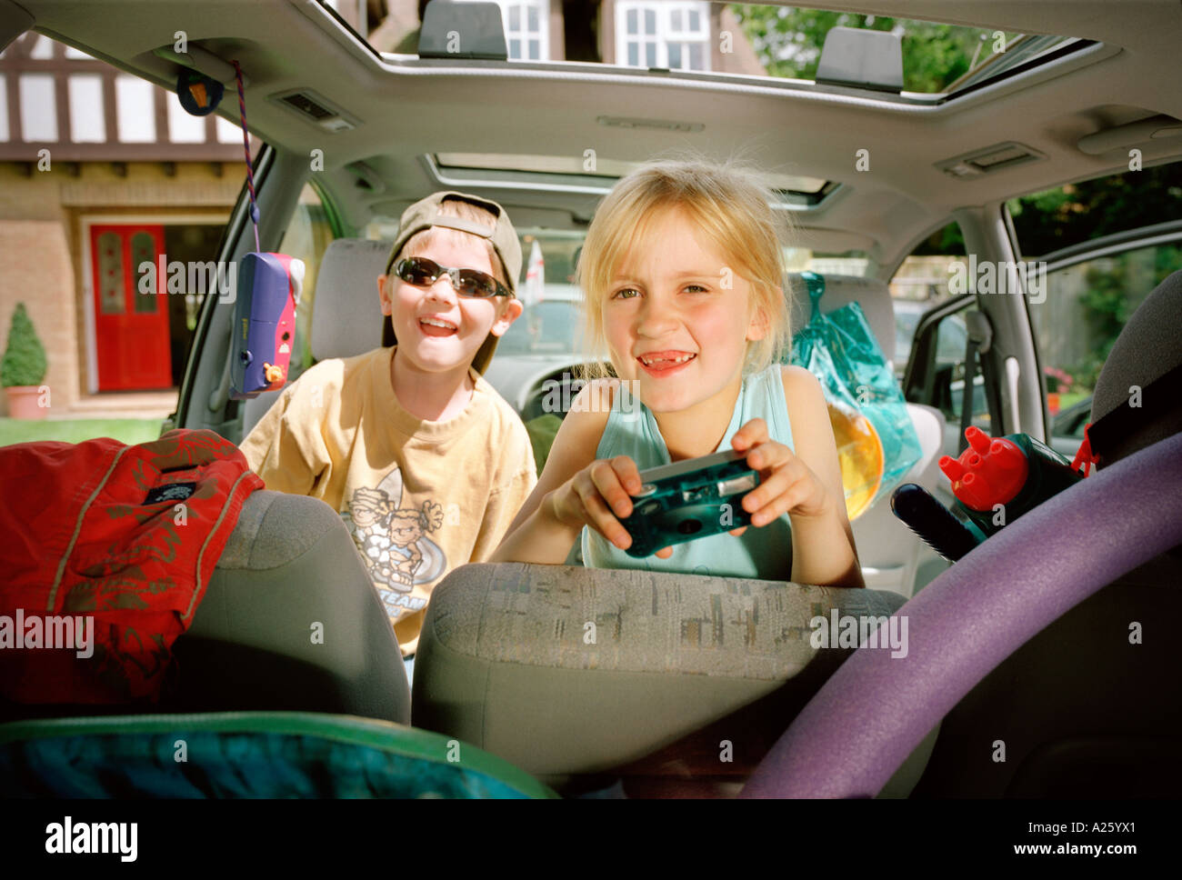 two excited children packing the car for a summer holiday smiling at ...