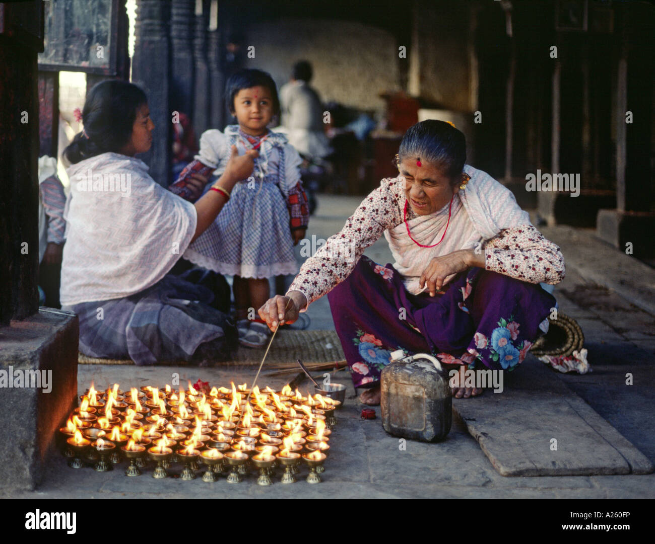 A NEWARI woman lights PUJA CANDLES at SWAYAMBUNATH STUPA KATHAMANDU ...