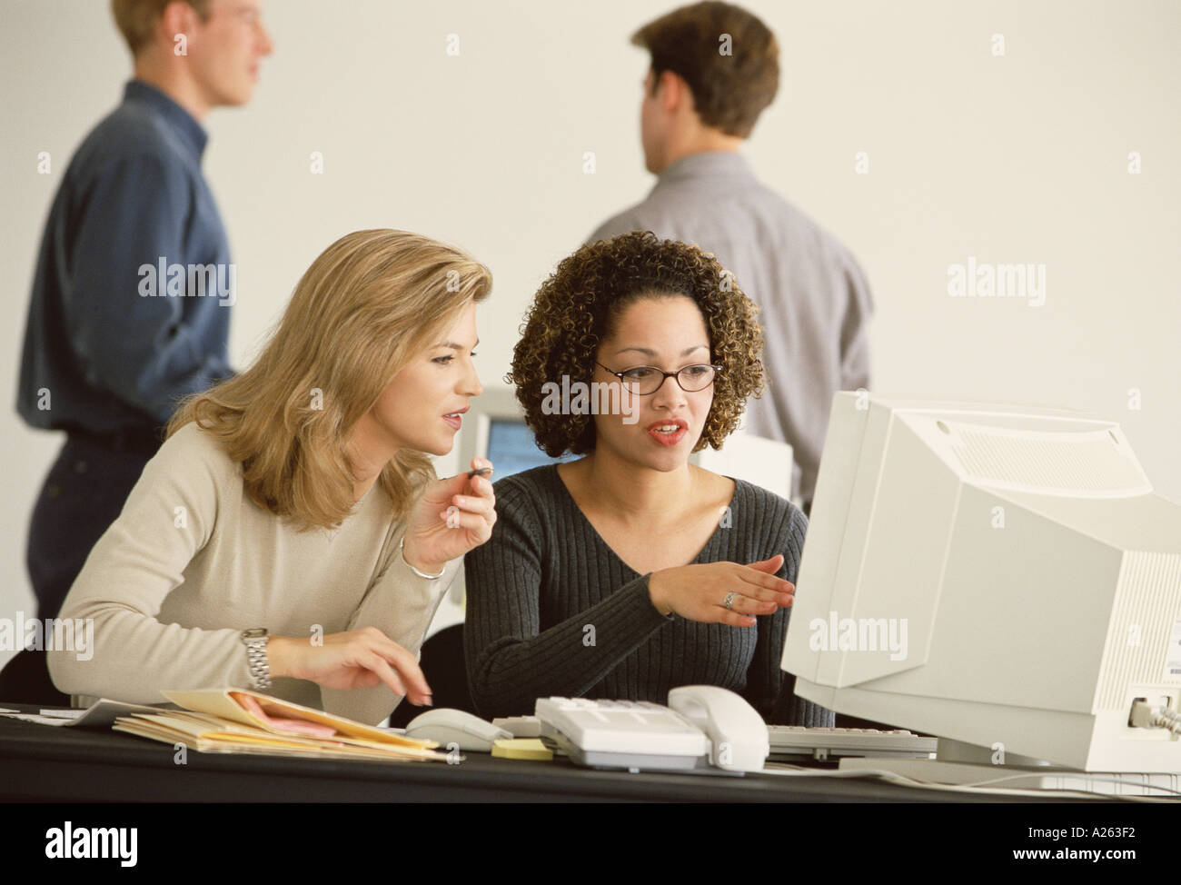 WOMEN LOOKING AT COMPUTER SCREEN IN OFFICE WITH TWO MEN TALKING Stock ...