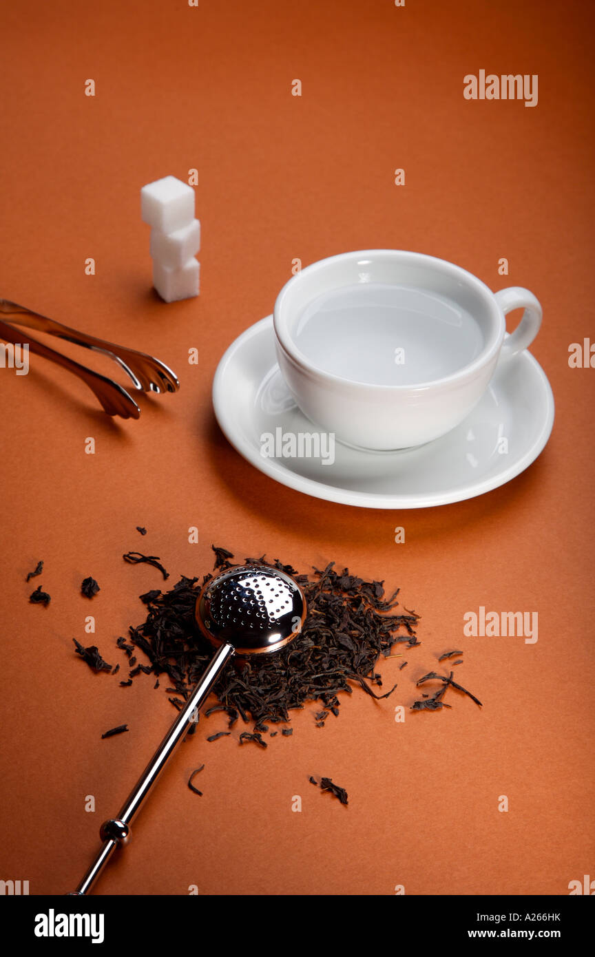 Spilled black tea leaves with strainer, sugar tongs, cup with water and ...