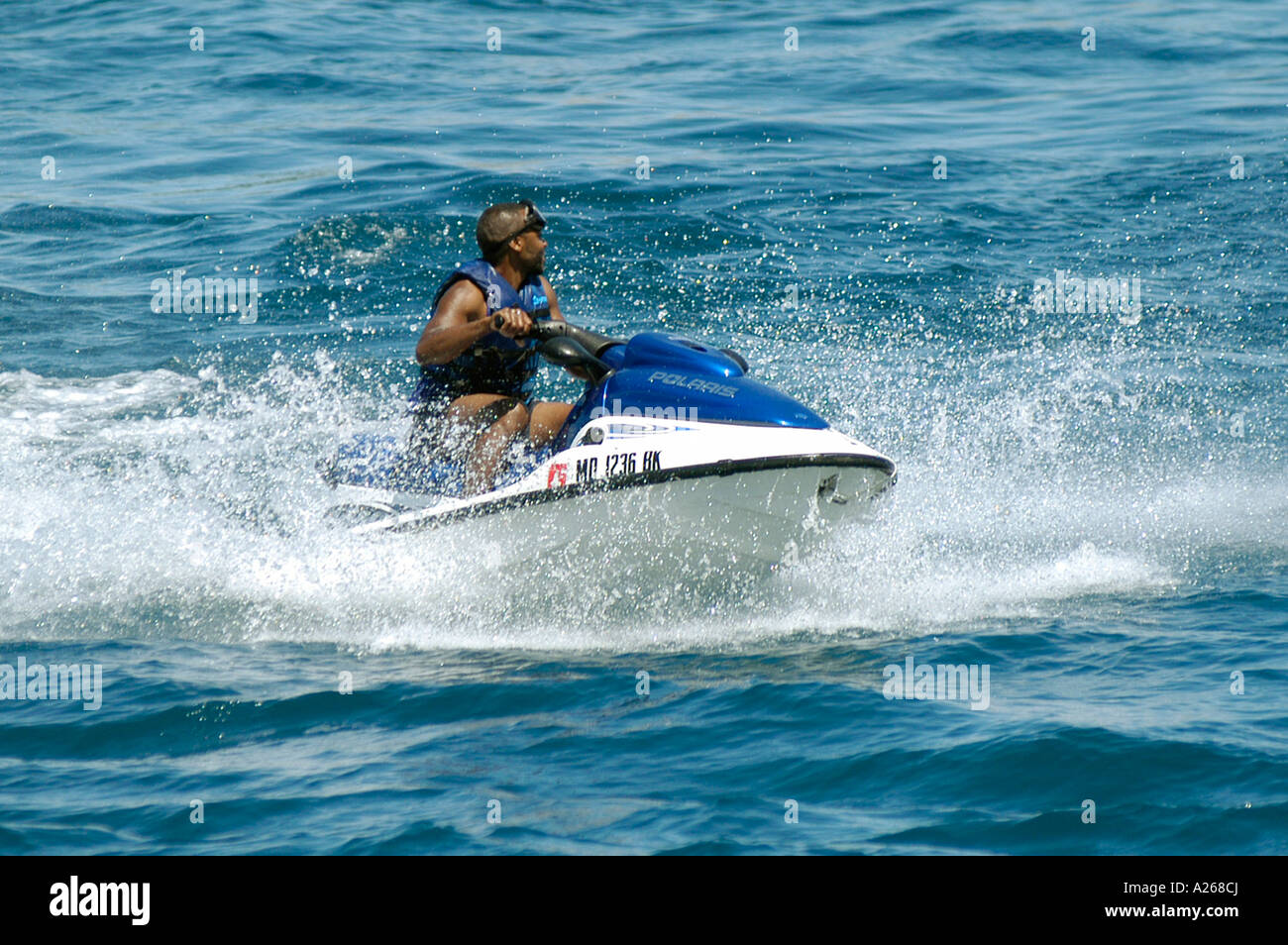 Black male wearing a life jacket performs maneuvers while riding a wave ...