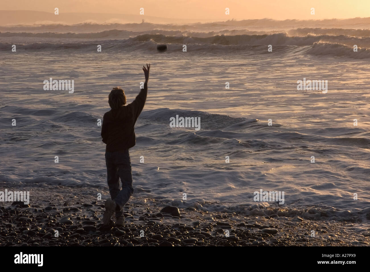 Figure throwing a stone into the sea at Sandymouth beach Cornwall ...