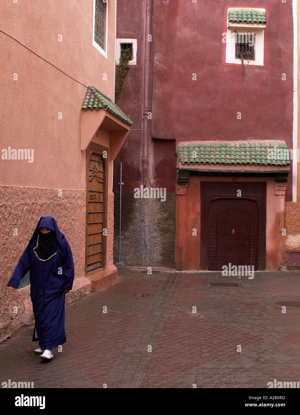 A Moroccan woman in traditional clothing walks through a back street of ...