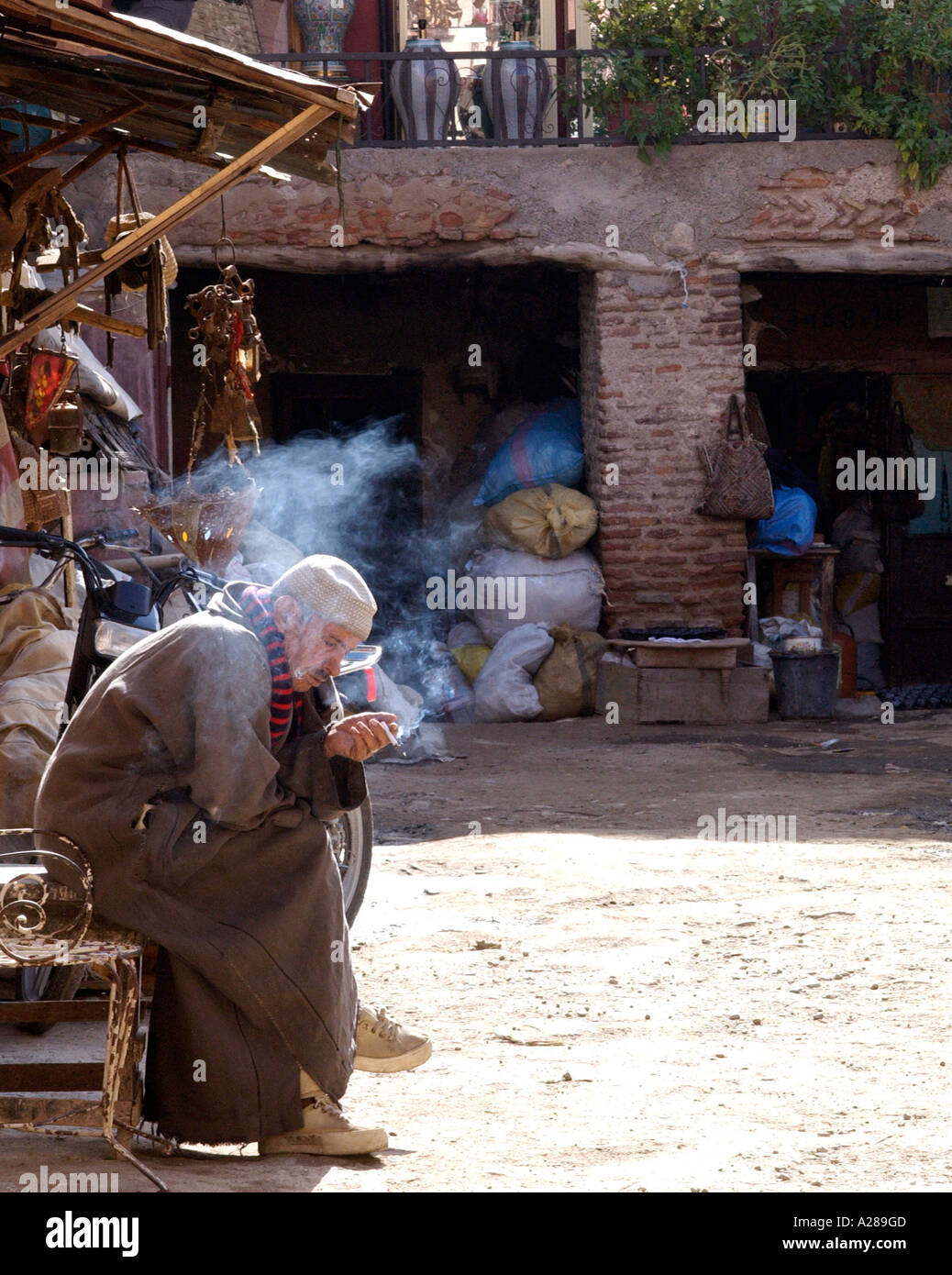 A Moroccan man in tradional clothing relaxes and has a smoke away from ...