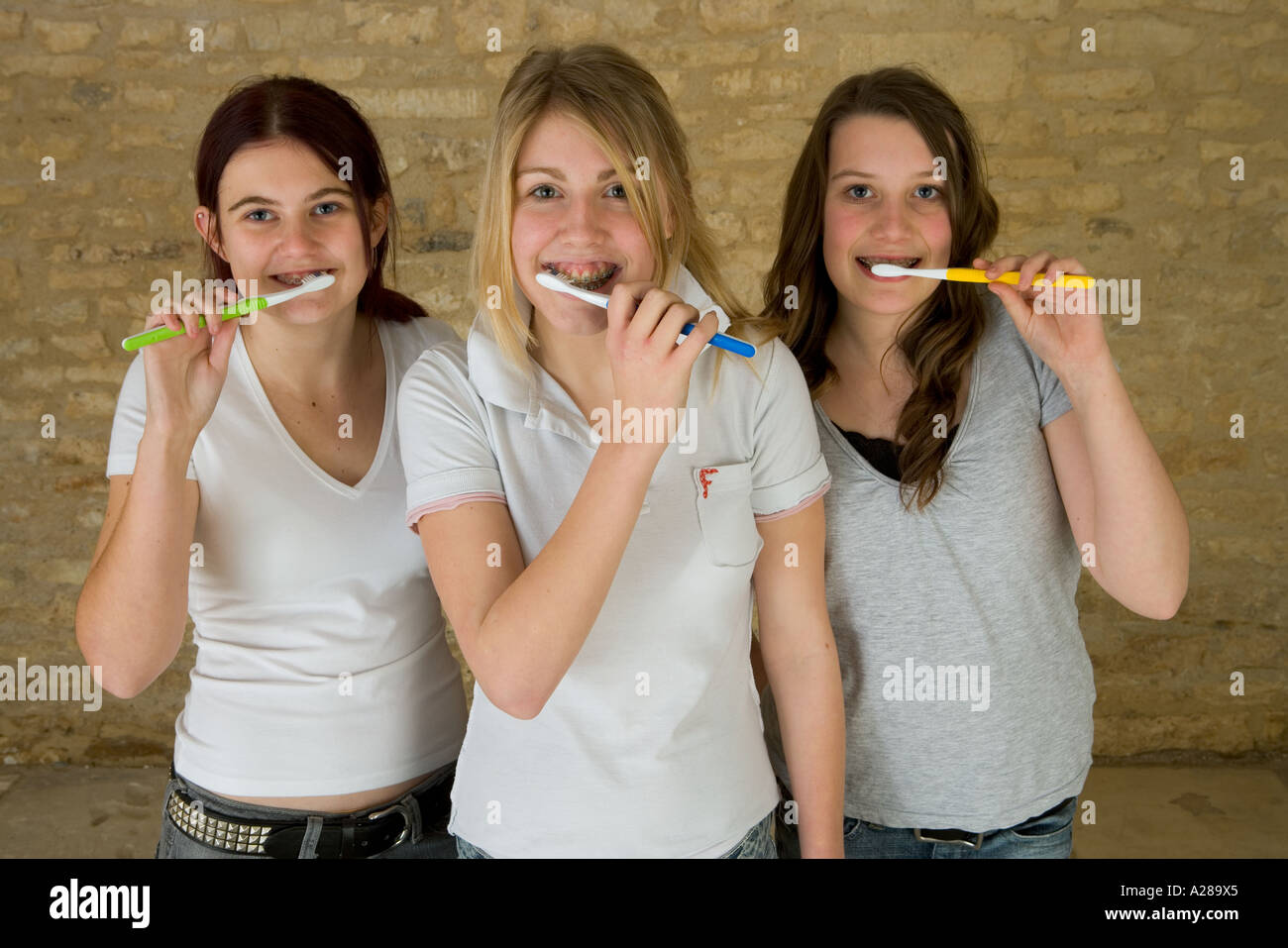 THREE TEENAGE GIRL FRIENDS WITH ORTHODONTAL BRACES BRUSHING THEIR TEETH ...
