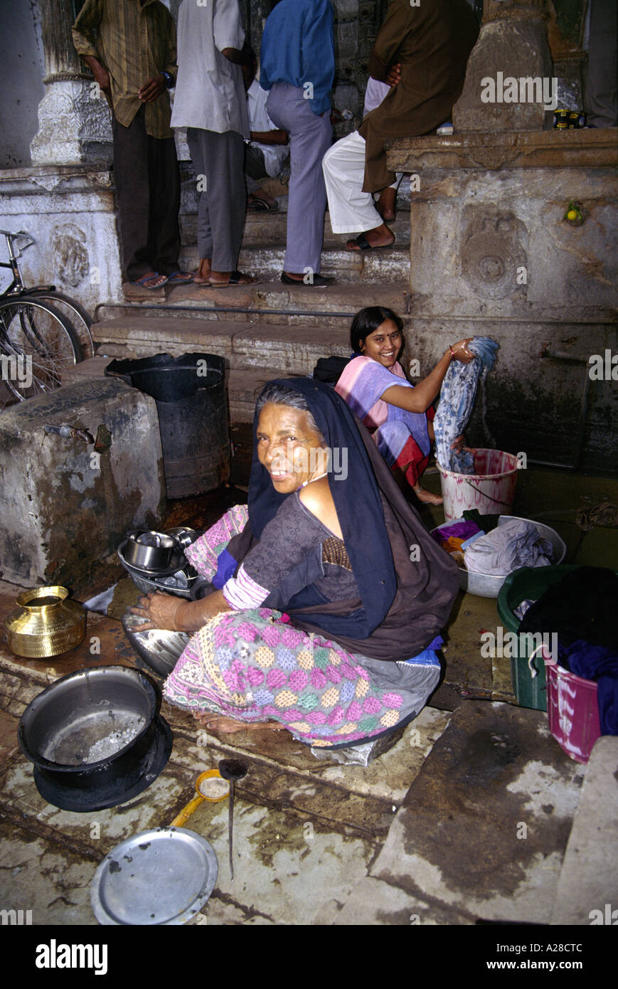 An Indian woman and girl wash pots and clothes while men stand idle ...