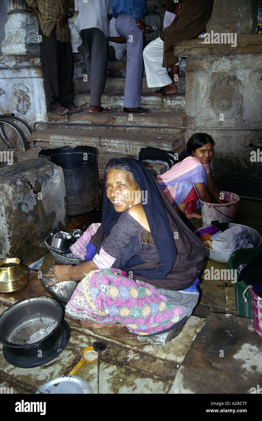 An Indian woman and girl wash pots and clothes while men stand idle ...