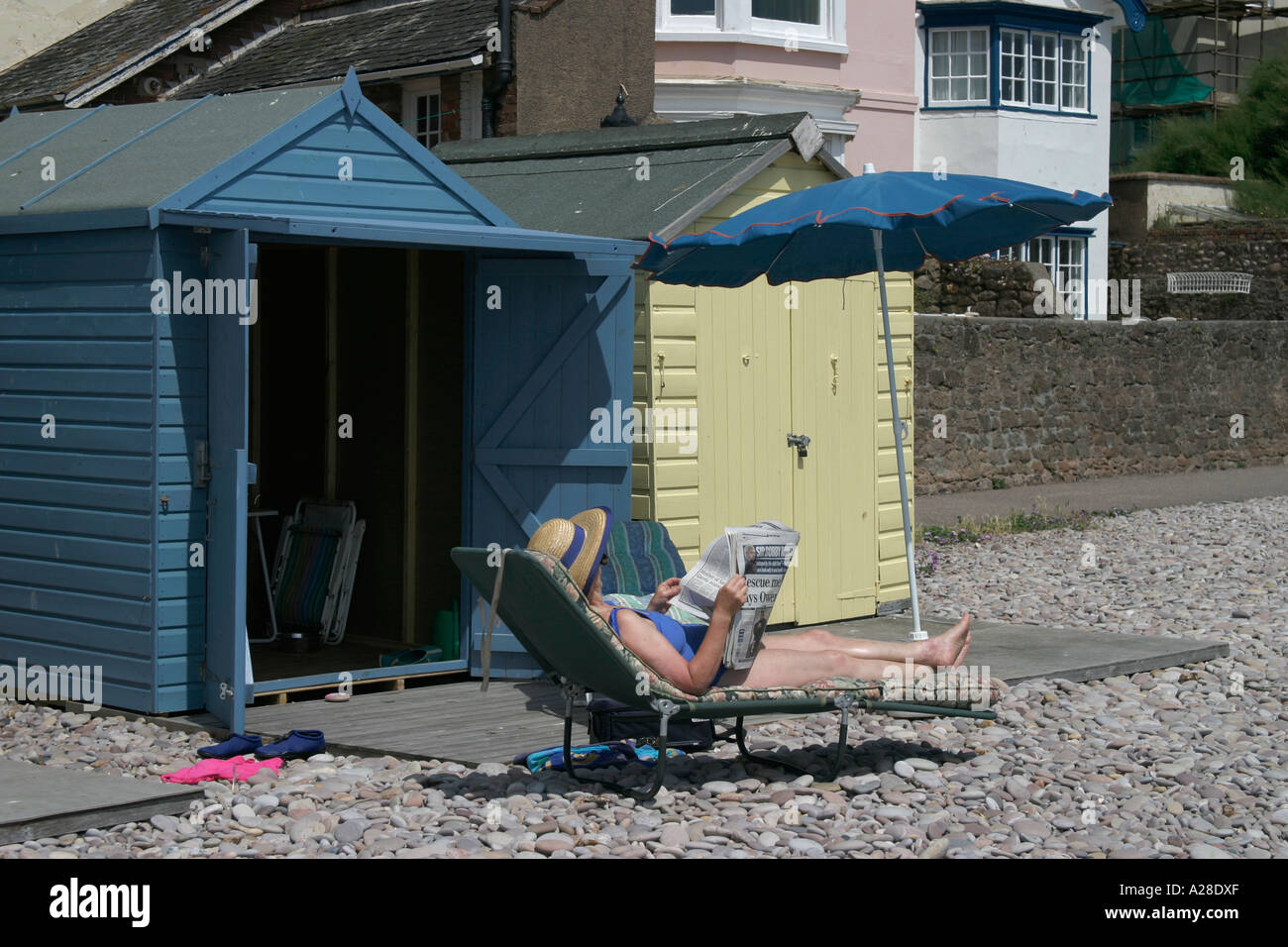 Lady reading tabloid newspaper at beach hut Budleigh Salterton Beach ...